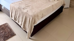 Quarto de hotel com cama, ar-condicionado fixado na parede, pequena geladeira e janela com cortinas.