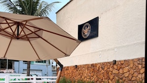 Área de piscina ao ar livre com parede de pedra, mesa e cadeiras, e um guarda-sol.