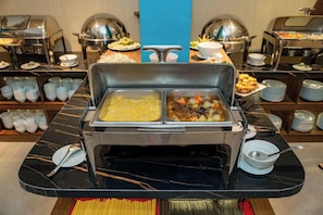 Disposição de buffet com dois recipientes: um com um prato amarelo e outro com um ensopado de legumes.