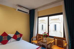 Quarto de hotel com cama, mesa com cadeiras, um vaso de flores e janela com cortinas.