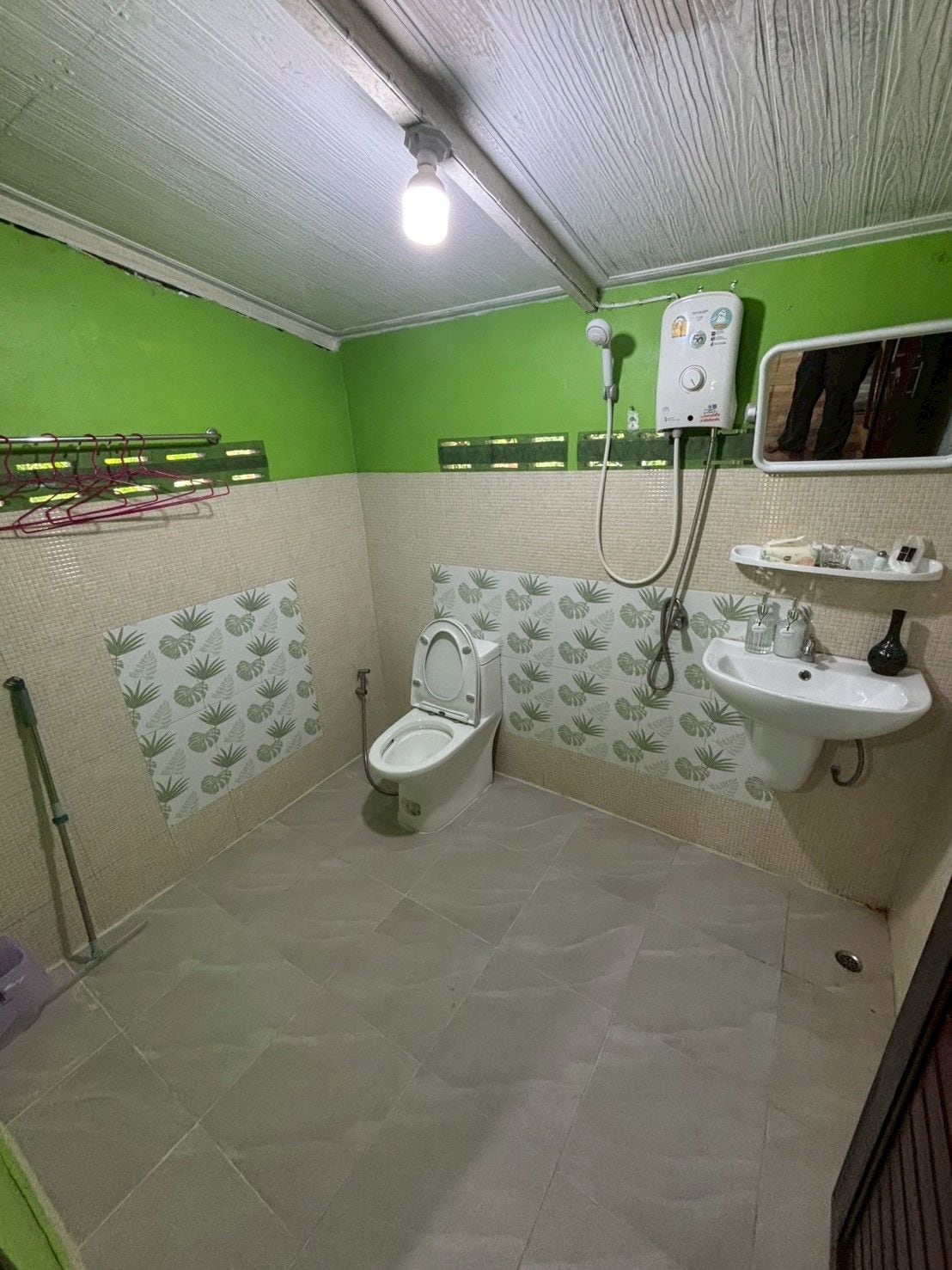Casa de banho com sanita, lavatório, chuveiro e paredes verdes.