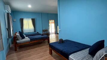 Quarto com duas camas de madeira, janela com cortinas, ventoinha no teto e piso de madeira.