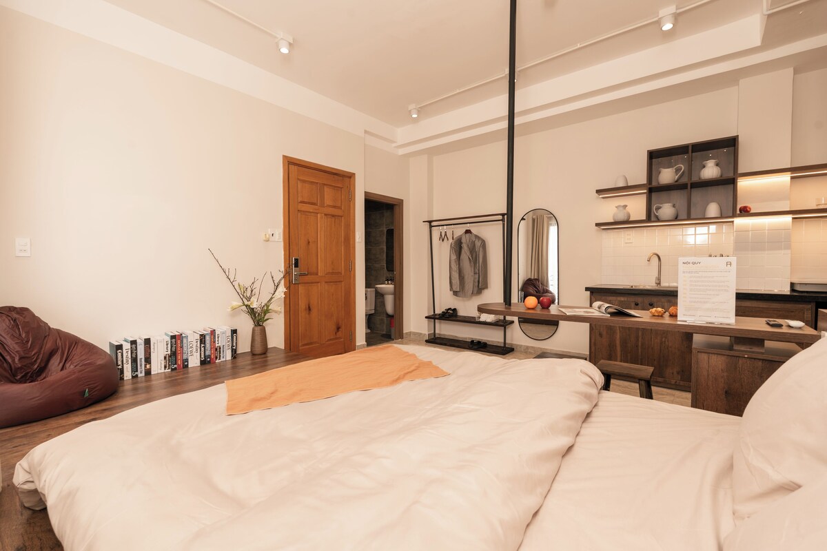 Quarto moderno com uma cama grande, porta de madeira, espelho, escrivaninha com computador e estante de livros.