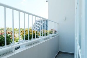 Varanda com grades brancas, vista de um edifício e diversas flores.