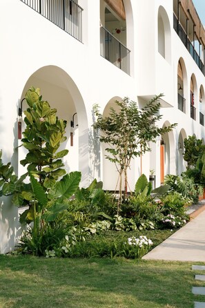 Um edifício com várias janelas em arco e um jardim bem cuidado, com diversas plantas e flores.