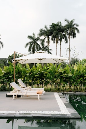 Uma área ao lado da piscina com espreguiçadeiras e um toldo.