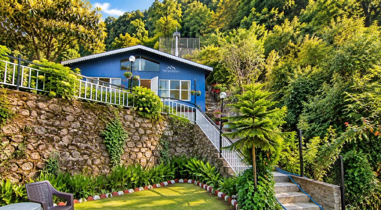 Edifício azul com parede de pedra, escadaria e jardim com uma cadeira.
