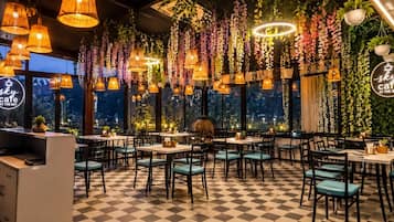 Interior de café com chão xadrez, plantas pendentes e iluminação pendular.