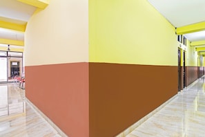 Um corredor com parede amarela e castanha, porta de vidro e um banco vermelho.