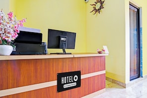 Bancada de recepção de hotel com computador, placa indicando hotel de serviço empresarial e um arranjo de flores.