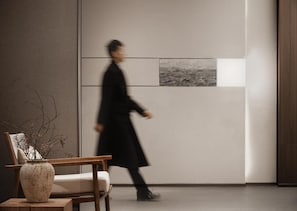 Um interior moderno com uma cadeira de madeira, um vaso com galhos e uma parede com uma obra de arte em preto e branco.