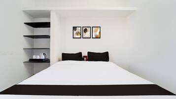 Quarto de hotel com uma cama, uma prateleira com chávenas e uma chaleira, e três quadros na parede.