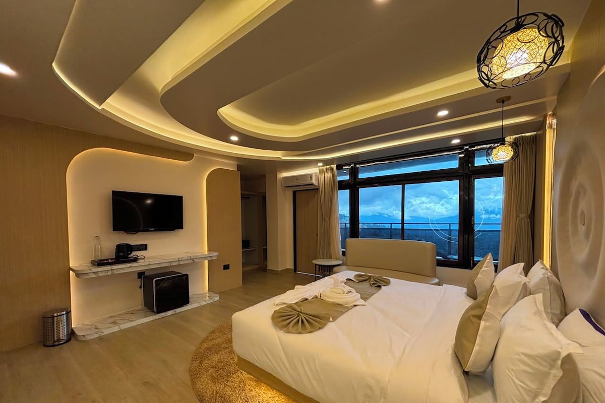 Quarto de hotel moderno com cama grande, televisão de tela plana, minibar e vista para o exterior.