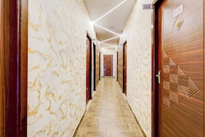 Corredor de hotel com paredes de mármore, portas numeradas e padrão de piso em espinha de peixe.