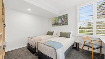 Quarto com duas camas, uma mesinha redonda, uma cadeira e uma janela com persianas.