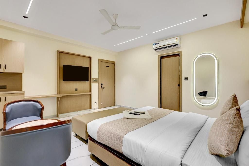 Quarto de hotel com cama, poltrona, televisão, aparelho de ar condicionado e ventoinha de teto.