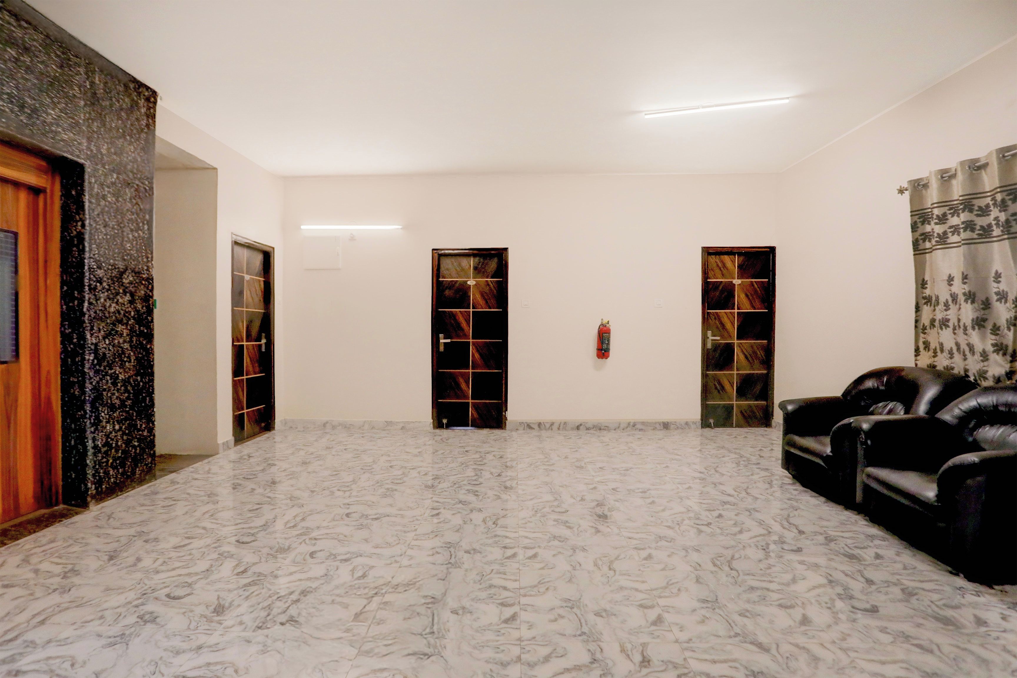 Quarto amplo com piso de mármore, sofá de couro preto e duas portas com painéis de vidro decorativos.