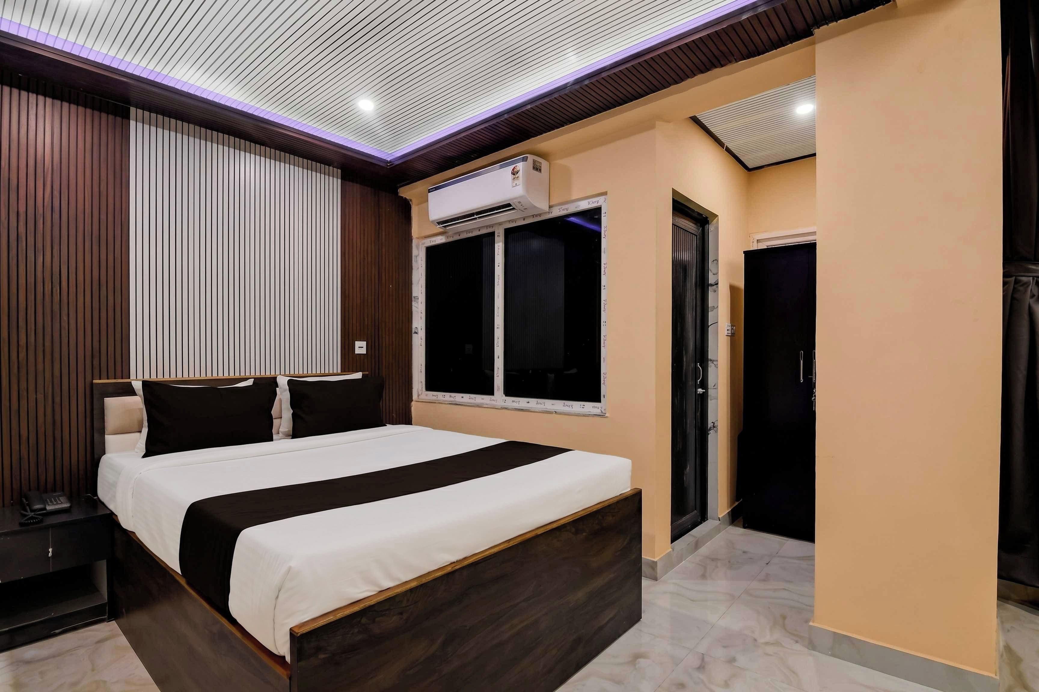 Quarto moderno com cama grande, mesa de cabeceira, ar condicionado fixado na parede e janela com persianas.