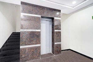 Um corredor com parede de mármore, uma porta e uma escadaria.