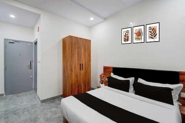 Quarto de hotel com uma cama, um guarda-roupa, uma porta e três quadros na parede.