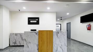 Balcão de recepção com tampos de mármore, painel de madeira e placa indicando serviço da empresa.