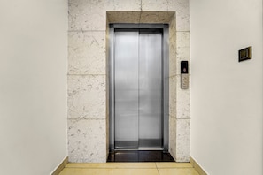 Um elevador com acabamento metálico, parede com padrão geométrico e chão em piso amarelado.