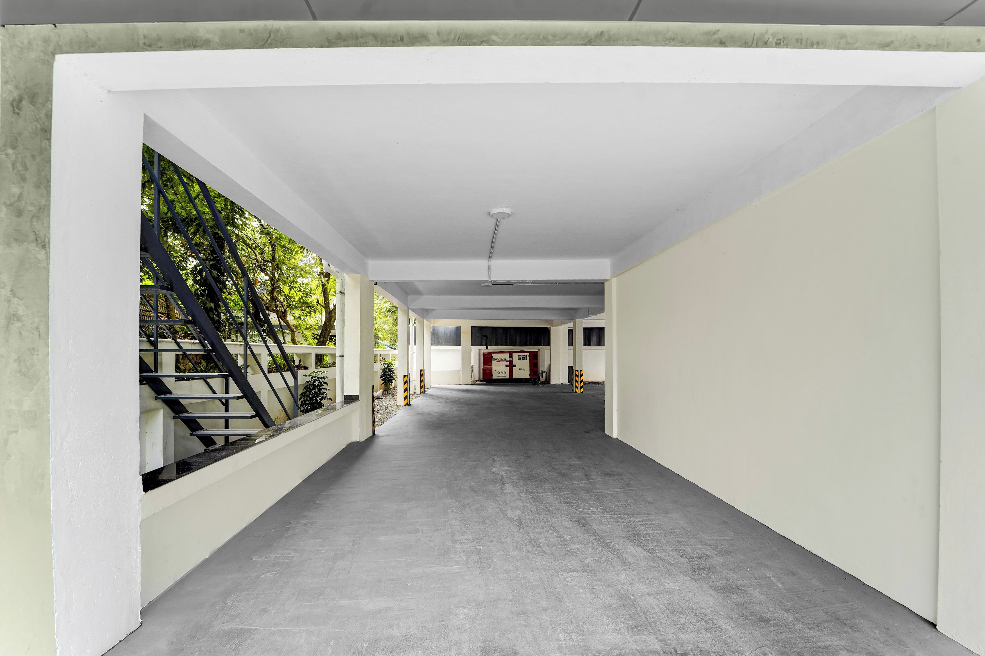 Um corredor com piso de concreto, paredes brancas e escada à esquerda.