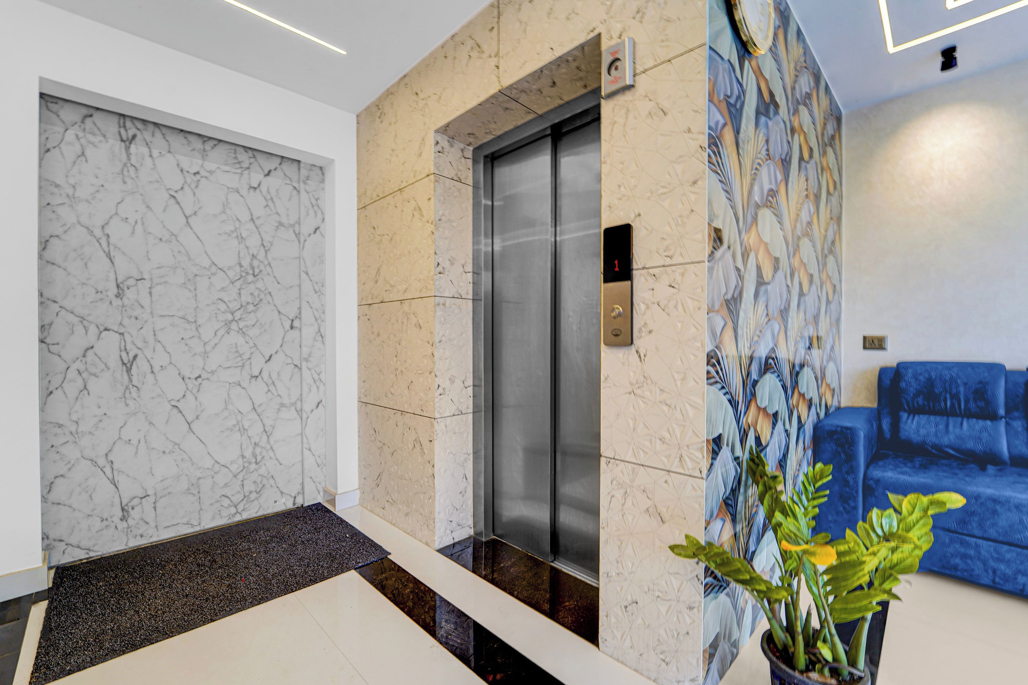 Um lobby moderno com parede de mármore, elevador, sofá azul e planta em vaso.