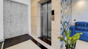 Um lobby moderno com parede de mármore, elevador, sofá azul e planta em vaso.