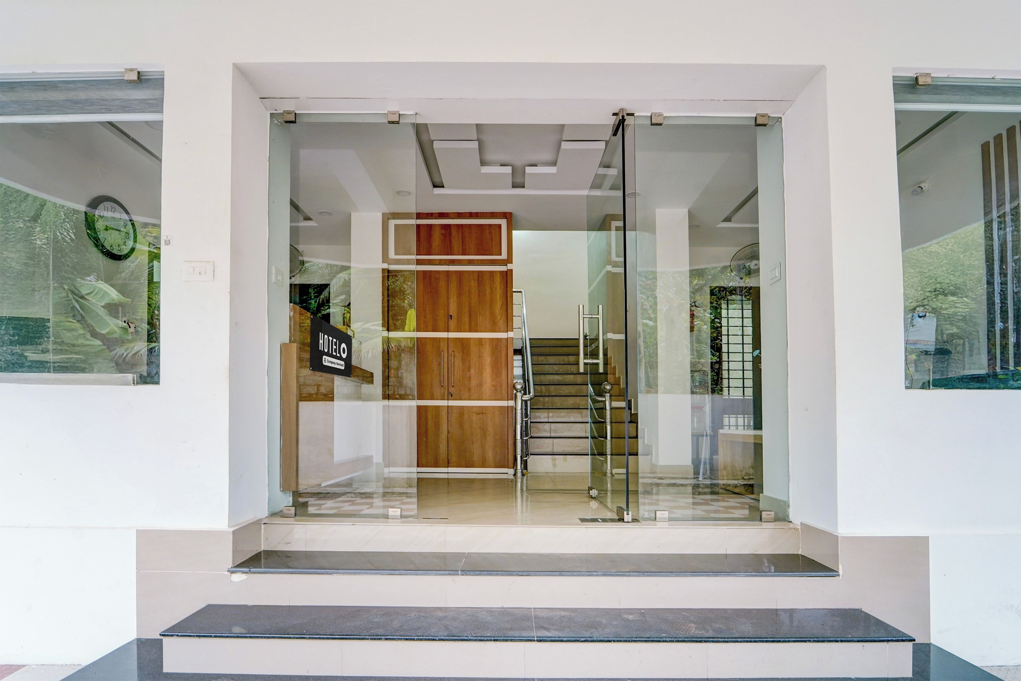 Entrada de hotel com porta de vidro, interior em madeira e escadaria interna.