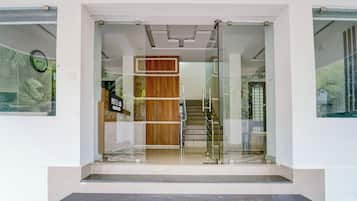 Entrada de hotel com porta de vidro, interior em madeira e escadaria interna.