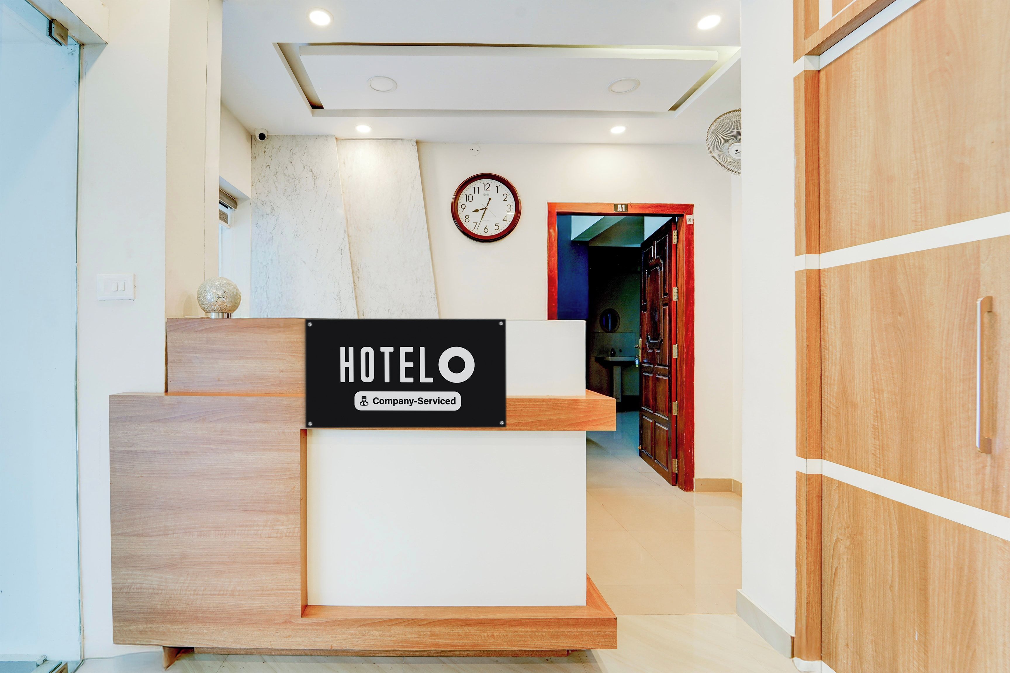 Bancada de recepção de hotel com uma placa indicando serviço corporativo. Há um relógio na parede e uma porta que dá para outro cômodo.