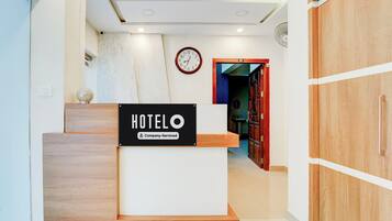 Bancada de recepção de hotel com uma placa indicando serviço corporativo. Há um relógio na parede e uma porta que dá para outro cômodo.