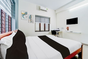 Quarto de hotel com cama, escrivaninha, cadeira, televisão e janela com persianas.
