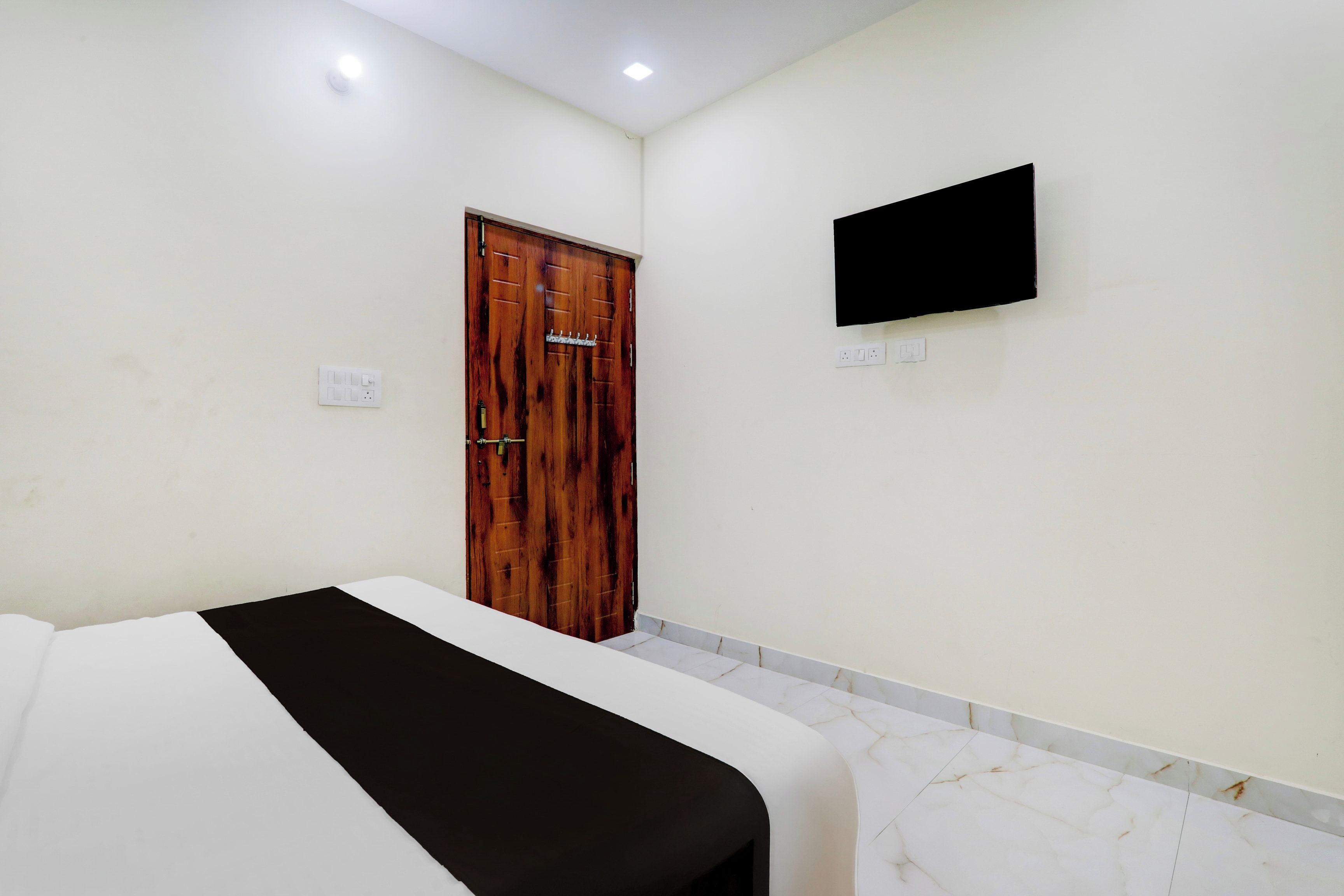 Quarto de hotel com cama, guarda-roupa de madeira, televisão na parede e chão de mármore branco.