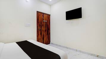 Quarto de hotel com cama, guarda-roupa de madeira, televisão na parede e chão de mármore branco.