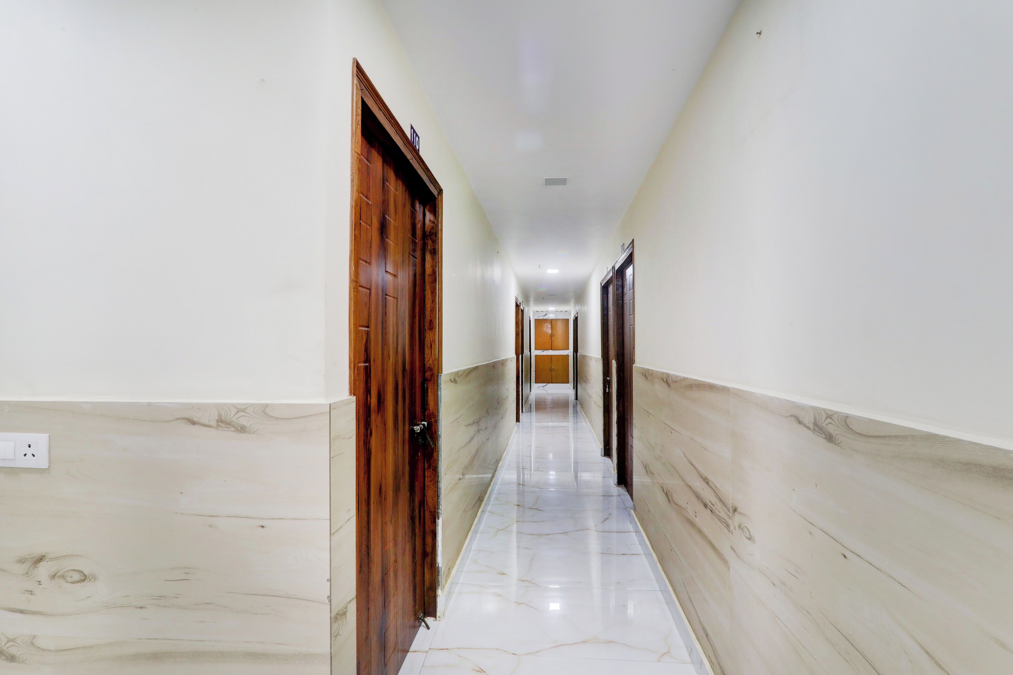 Um corredor com piso de mármore, portas de madeira e um acesso a um quarto com porta de madeira.