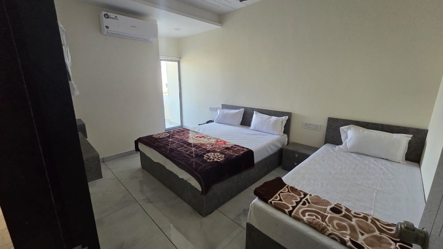 Quarto de hotel com duas camas, uma janela e aparelho de ar condicionado.
