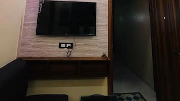 Uma sala de estar moderna com uma TV de tela plana fixada em uma parede texturizada, um sofá escuro, uma mesa de centro com dispositivos eletrônicos e uma porta de madeira.