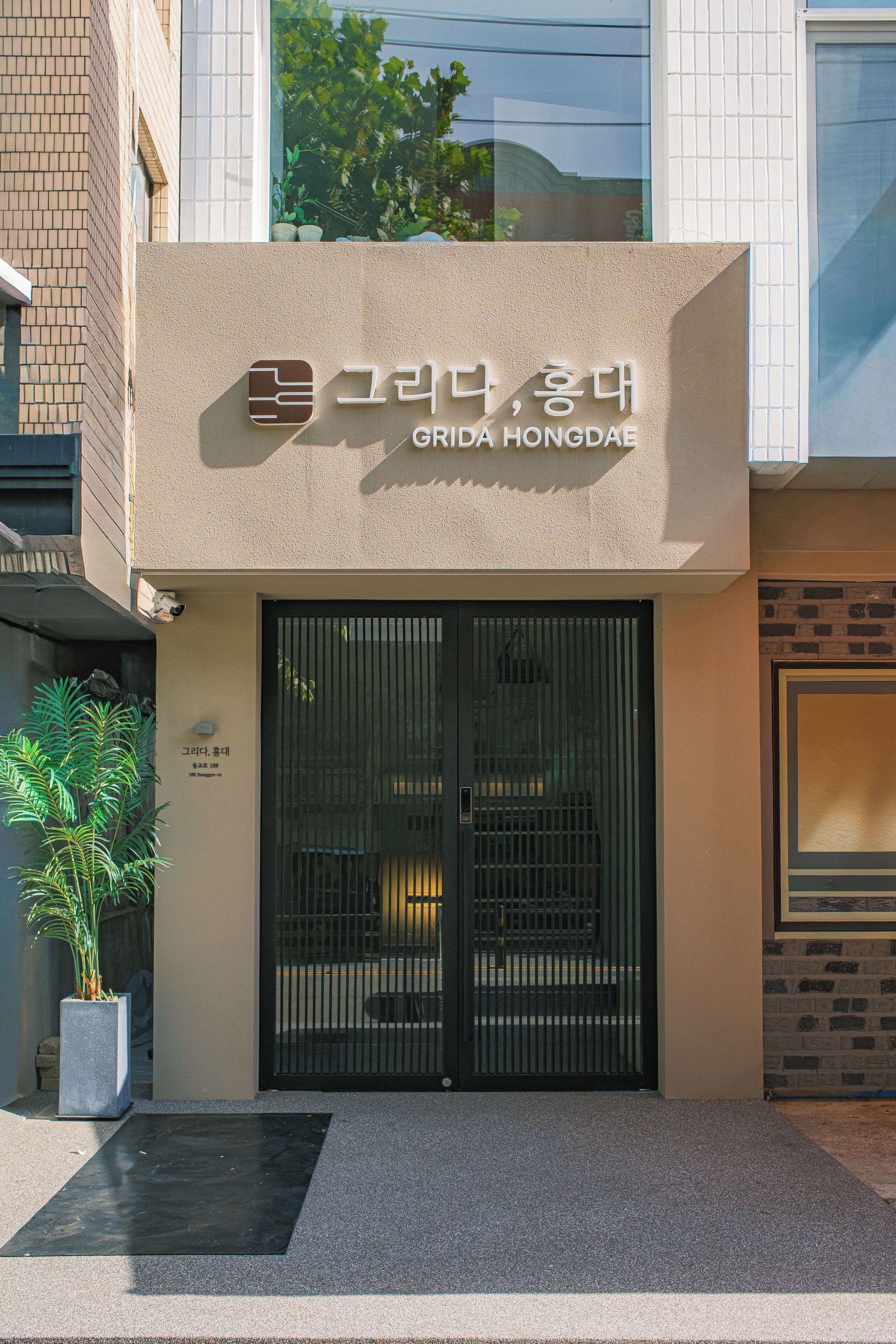 Entrada de um edifício com uma placa indicando 'GRIDA HONGDAE' e um portão.