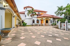 Um pátio espaçoso com piso de azulejos, um edifício branco com telhado de telhas vermelhas e palmeiras.