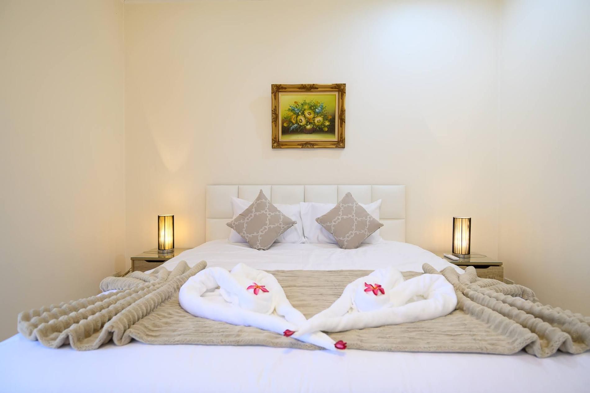 Quarto de hotel com cama, almofadas, um quadro e duas luminárias de cabeceira.