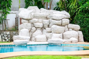 Piscina com parede de rocha e parede de pedra ao fundo.