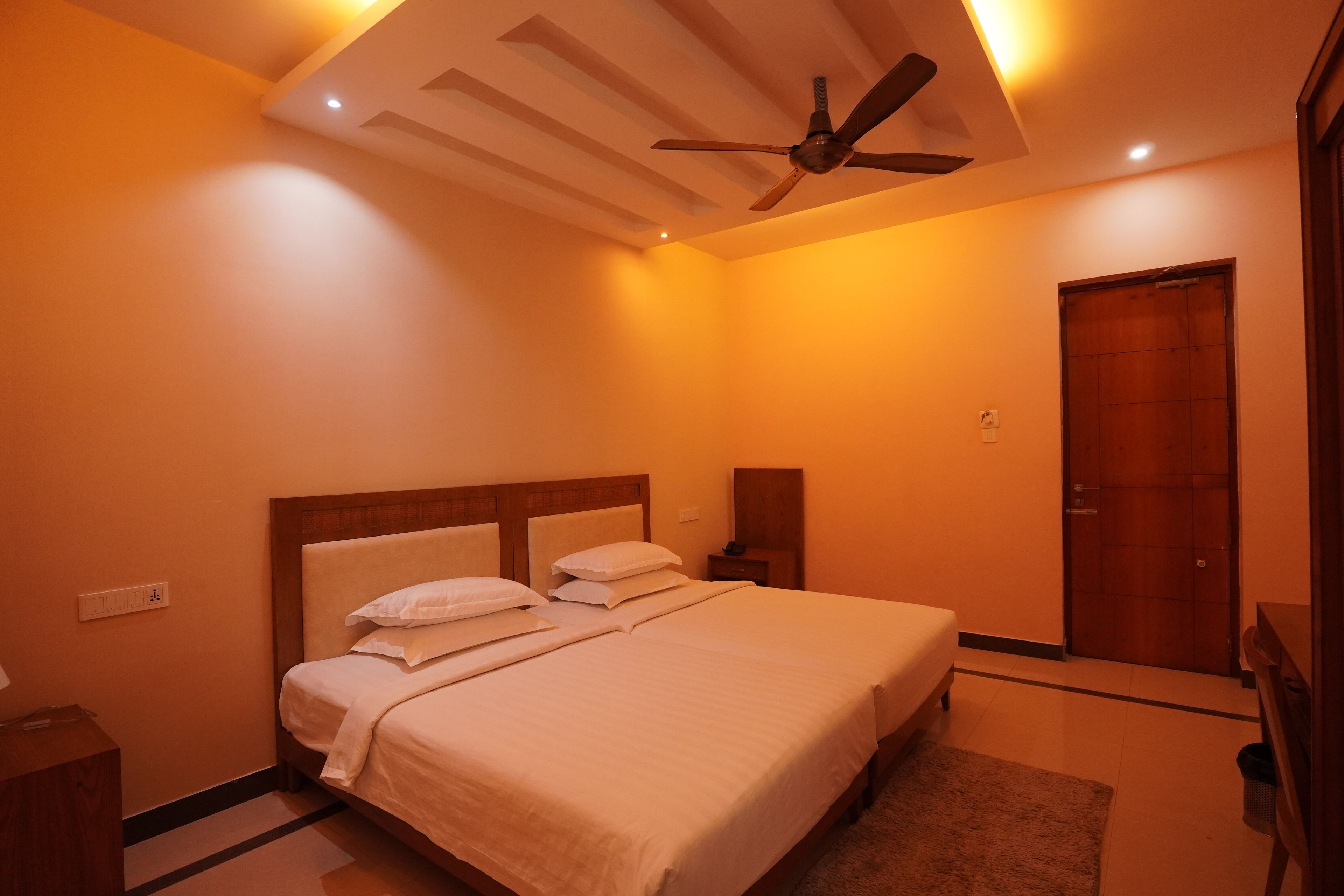 Quarto de hotel com cama, mesas de cabeceira, ventilador de teto e porta.