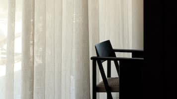 Quarto com cadeira e janela com cortinas leves.