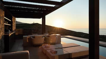 Área de estar ao ar livre com boa iluminação, paredes de pedra, piscina e vista para o mar.