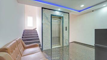 Um hall com piso de mármore, área de espera com poltronas de couro, escada e elevador.