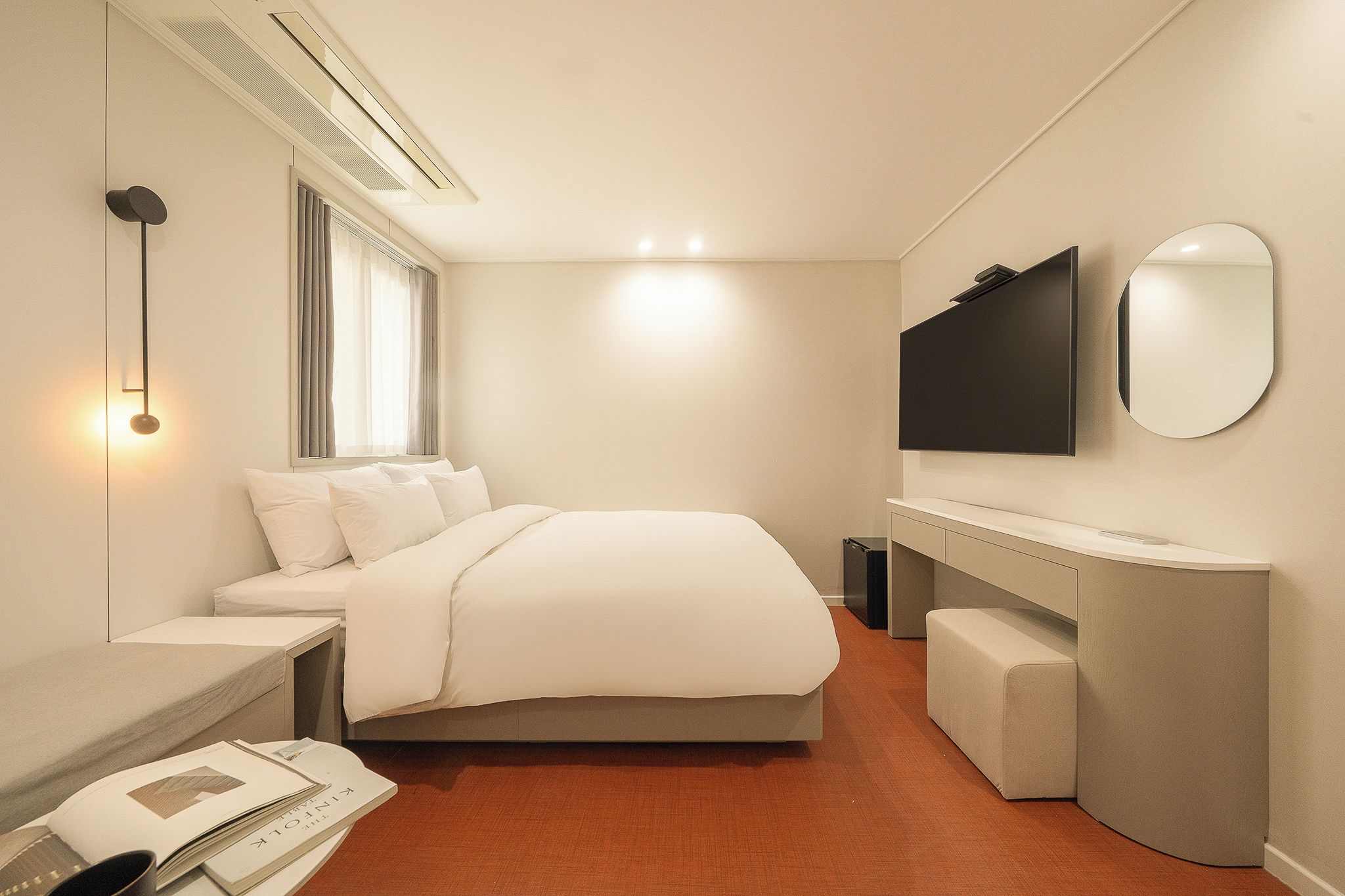 Quarto moderno com cama, mesa de cabeceira, luminária, TV e espelho.
