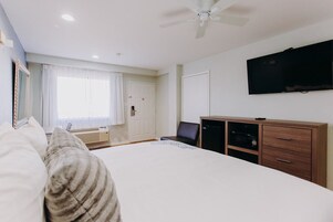 Quarto de hotel com uma cama, televisão, armário de madeira e ventoinha no teto.