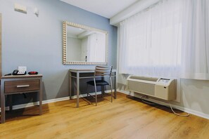 Quarto com escrivaninha, cadeira, espelho e janela com cortinas.